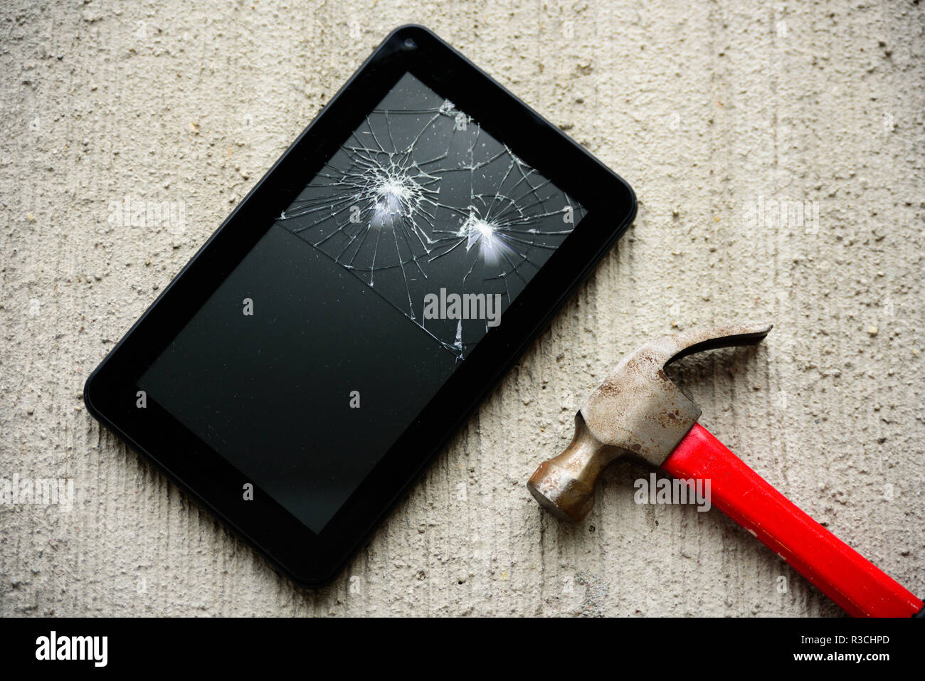 Broken tablet screen with red rusty hammer near it on concrete ...