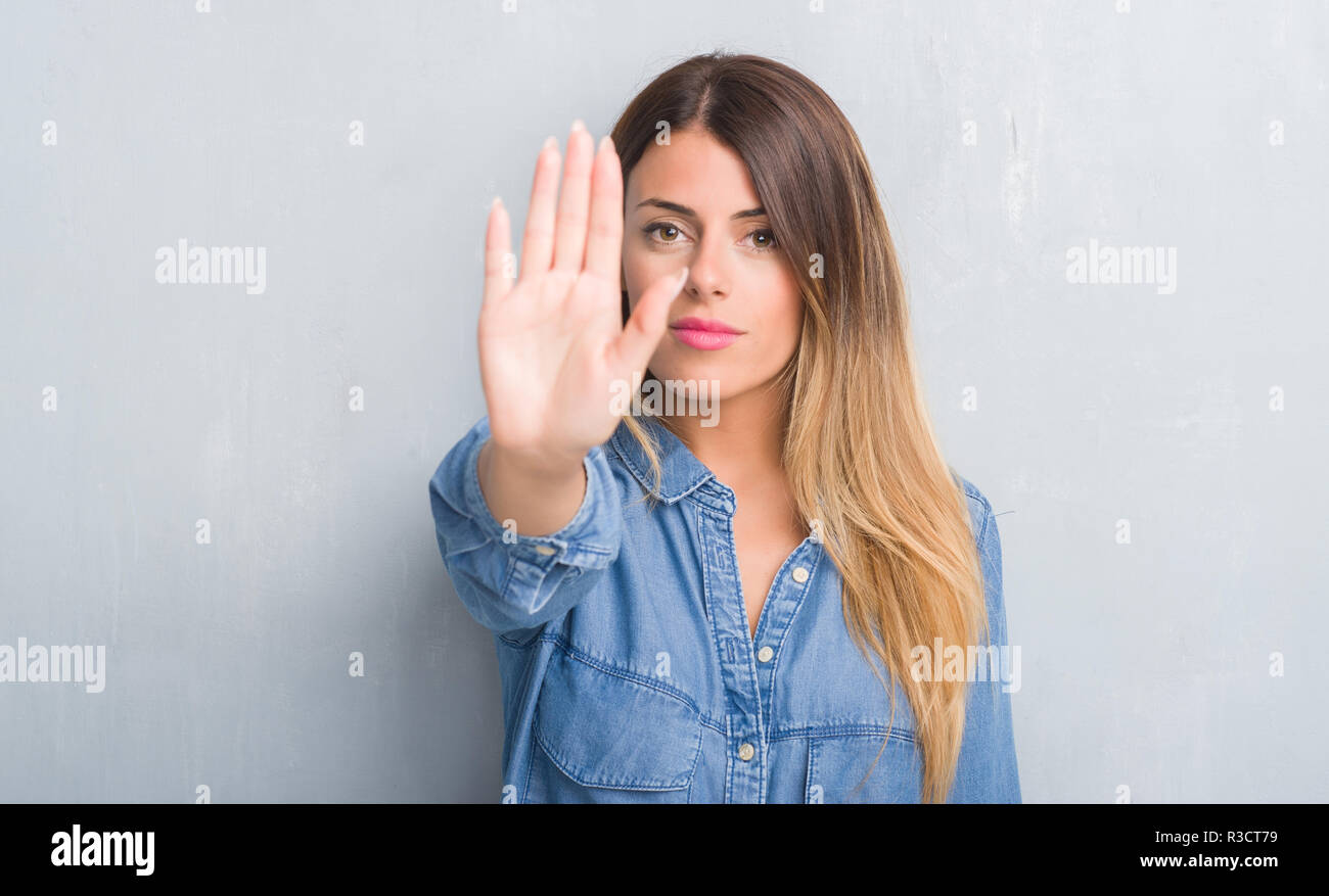 Young adult woman over grey grunge wall wearing denim outfit with open ...