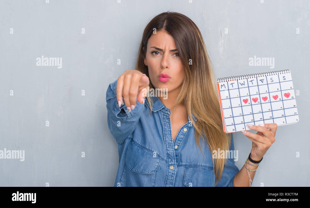 Young adult woman over grey grunge wall showing period calendar ...
