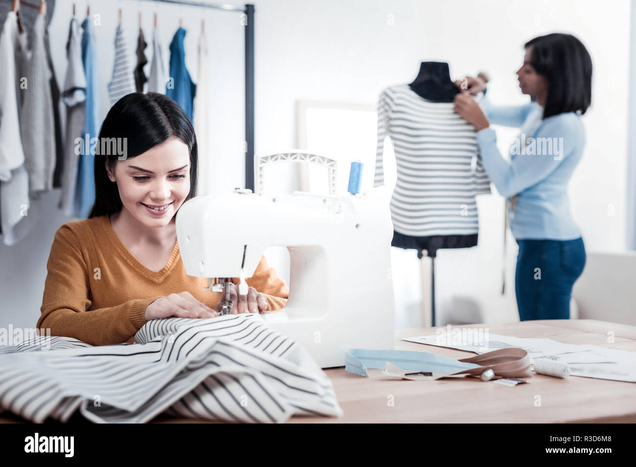 Skilled dressmaker. Cheerful positive woman sewing a dress while being ...