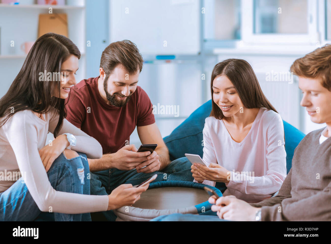 Total digitalization. Merry four friends using gadgets and staring at ...