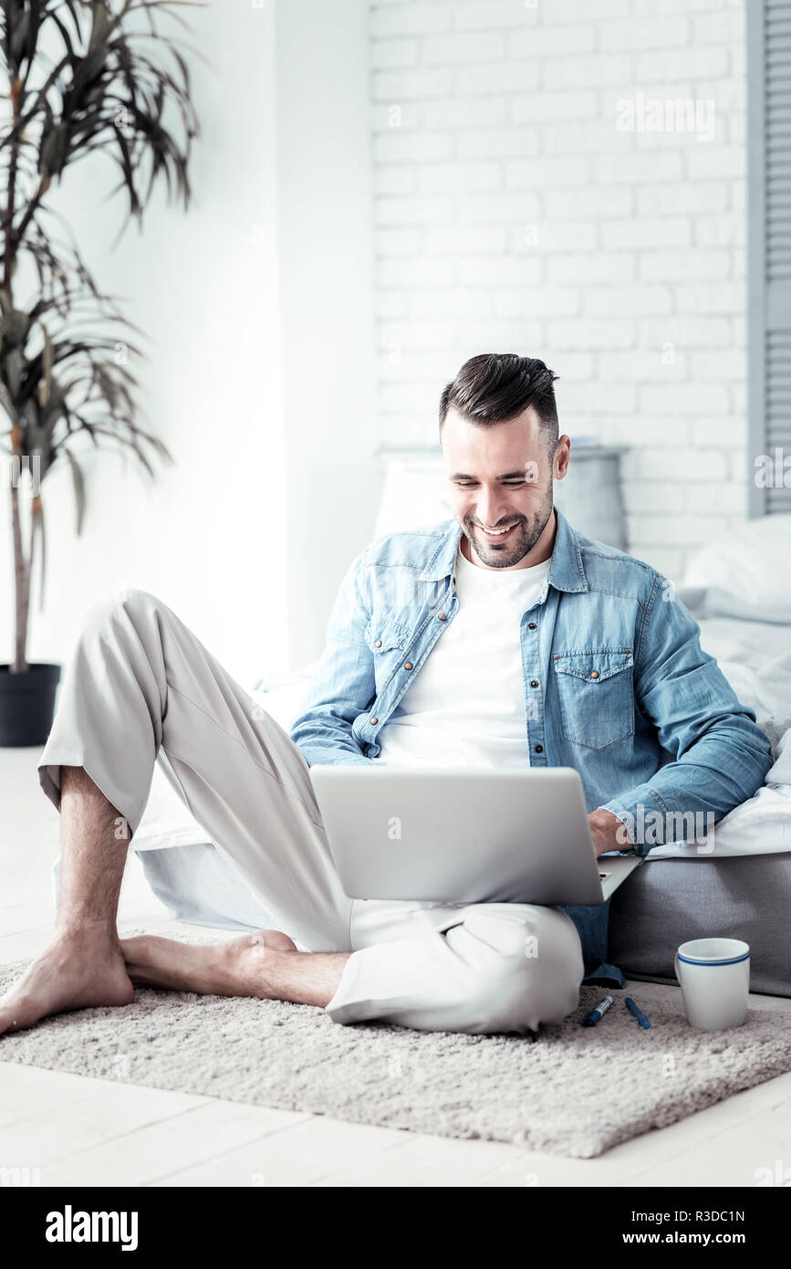It is my job. Cheerful male person holding laptop on legs and bowing ...