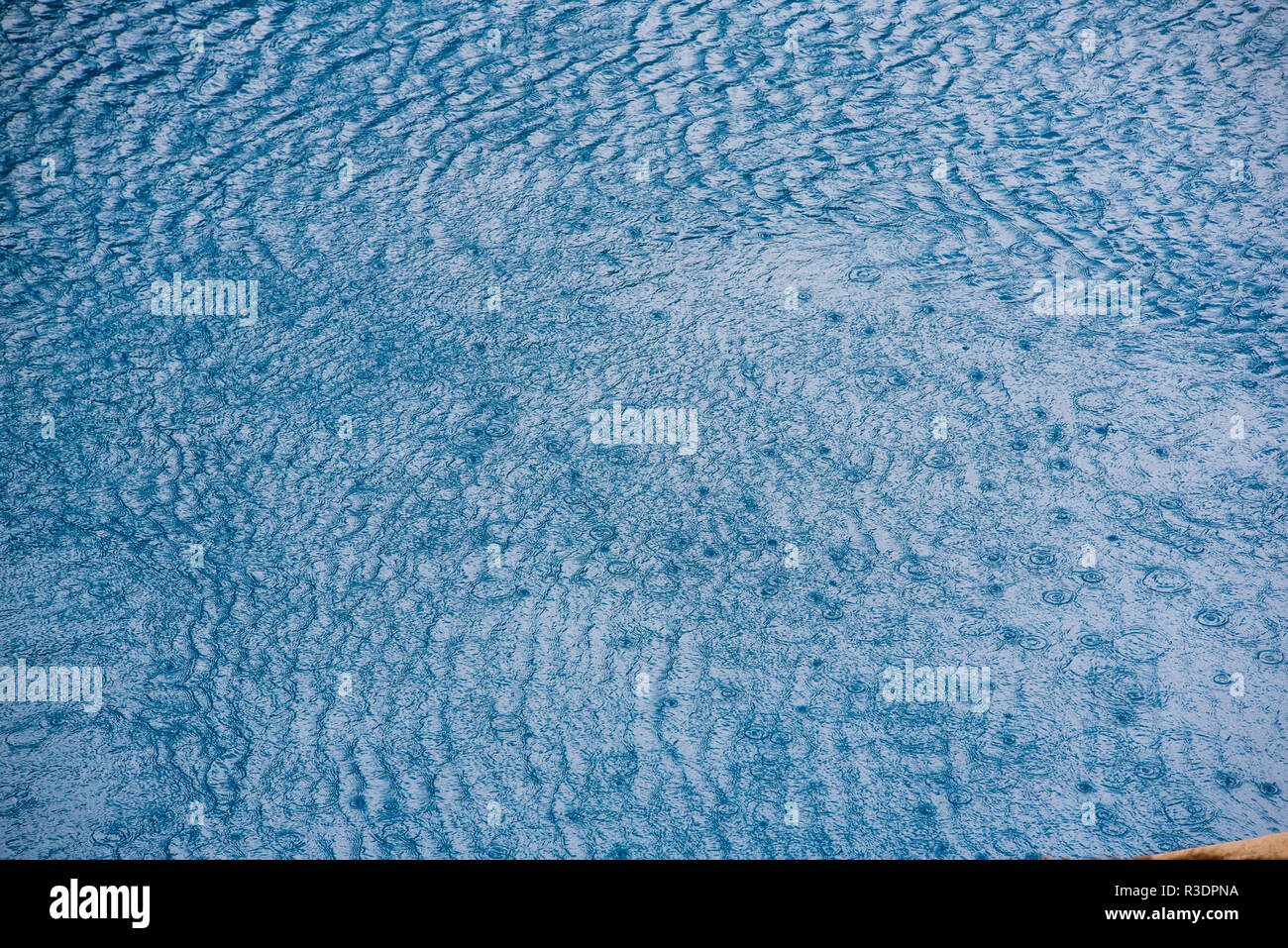 Water with small waves and raindrops on a pool with blue texture ...