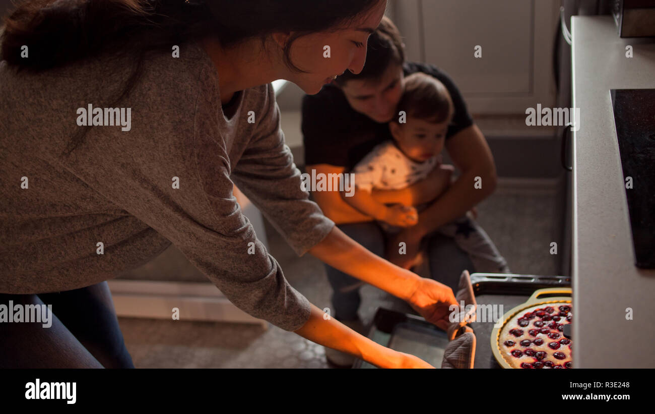 young multiethnic family making a cake together. Mom dad and son pull ...