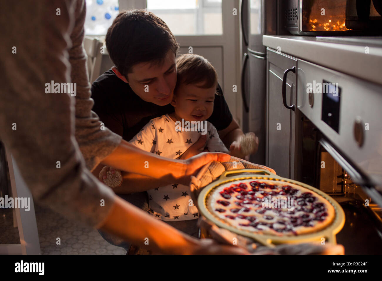 young multiethnic family making a cake together. Mom dad and son pull ...