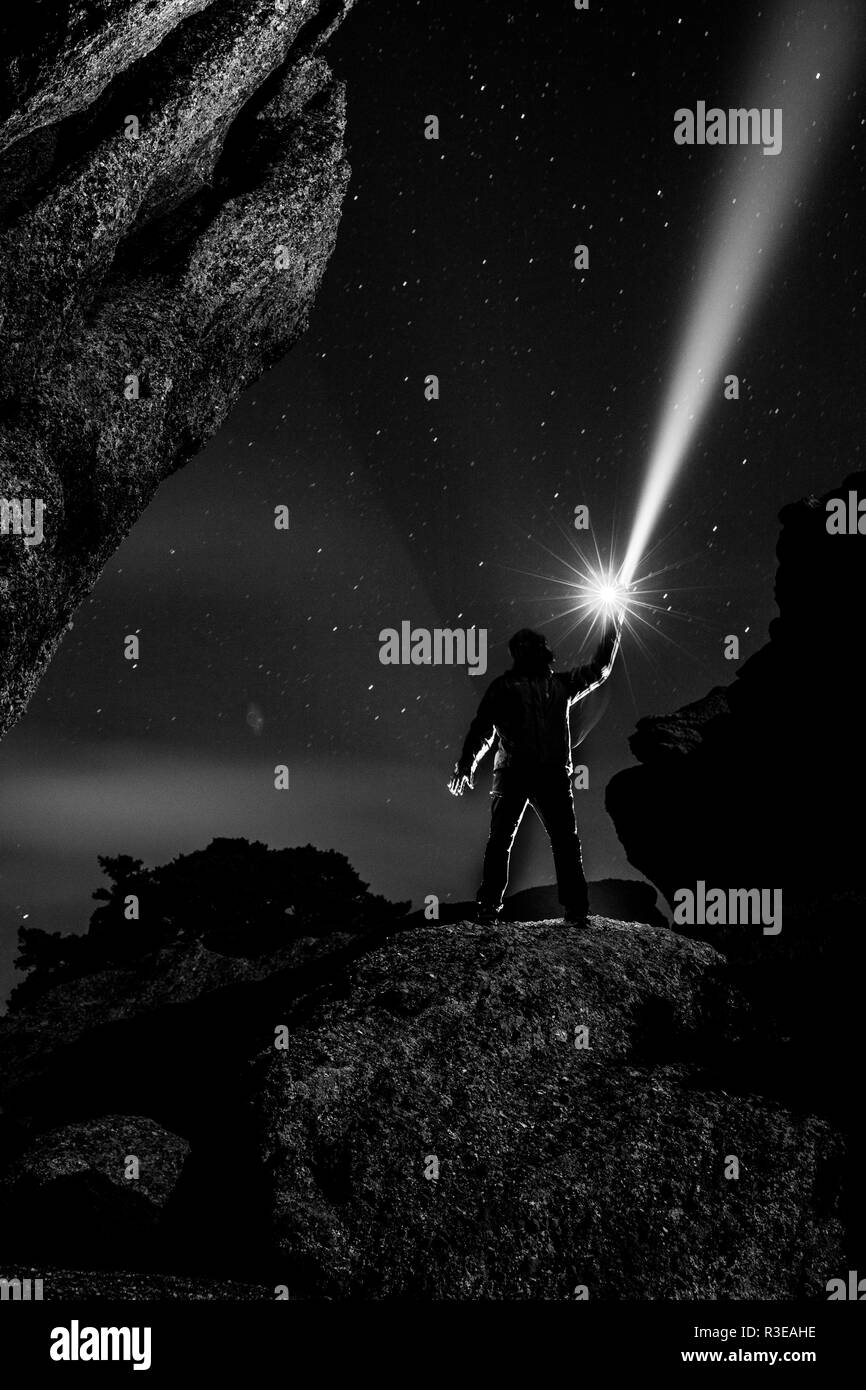 Man on a rock illuminating the dark night sky with a very powerful ...