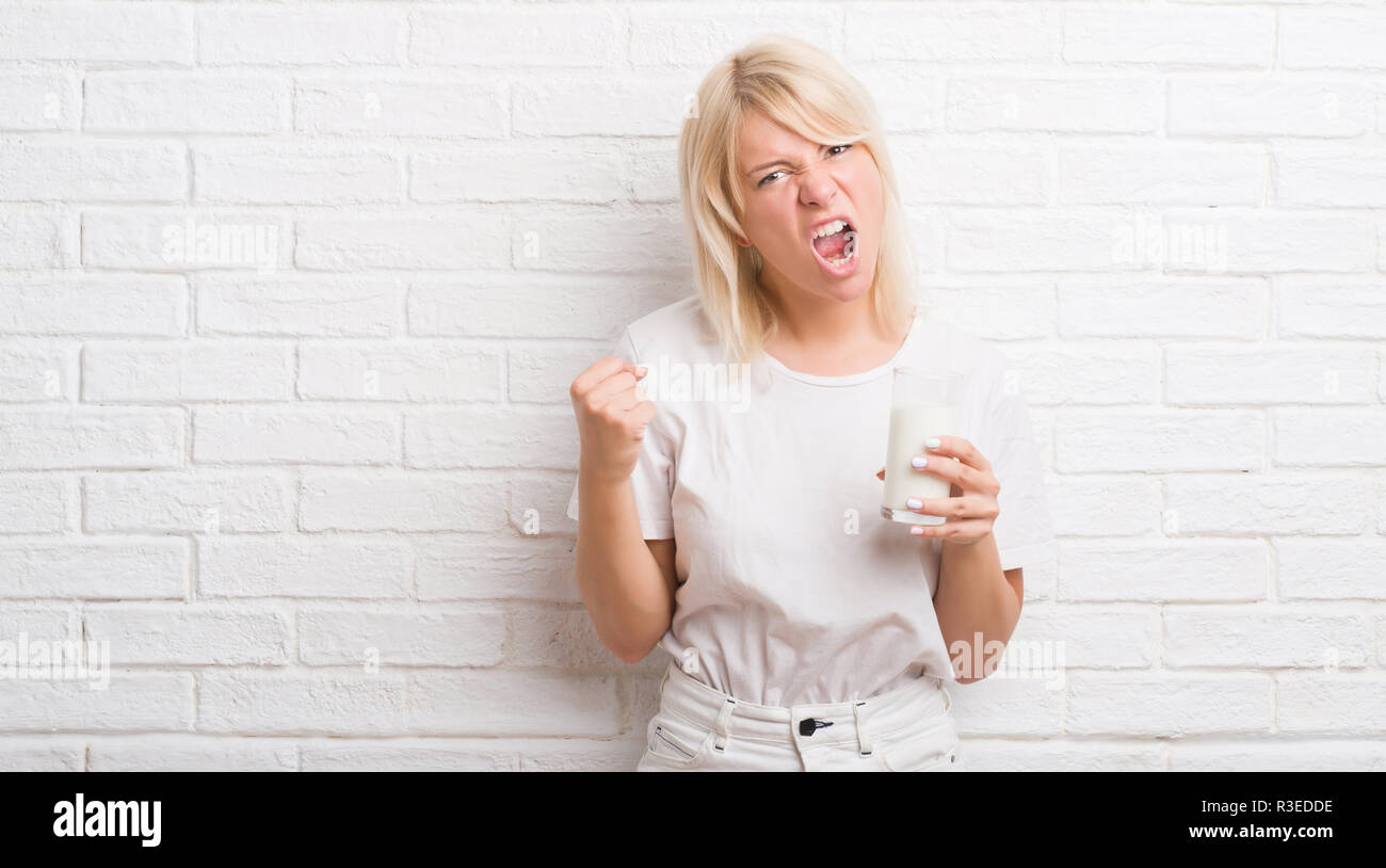 Adult caucasian woman over white brick wall drinking glass of milk ...