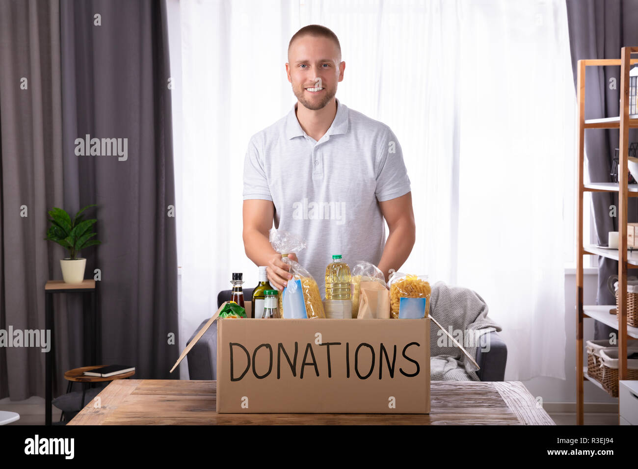 Young Man Putting Groceries In Donation Box Over Wooden Desk Stock ...
