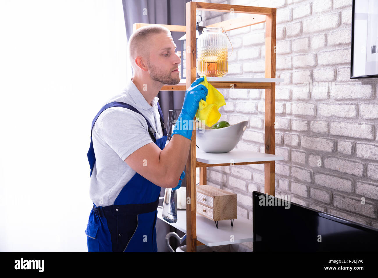 Side View Of A Young Male Janitor Cleaning Shelf In House Stock Photo ...
