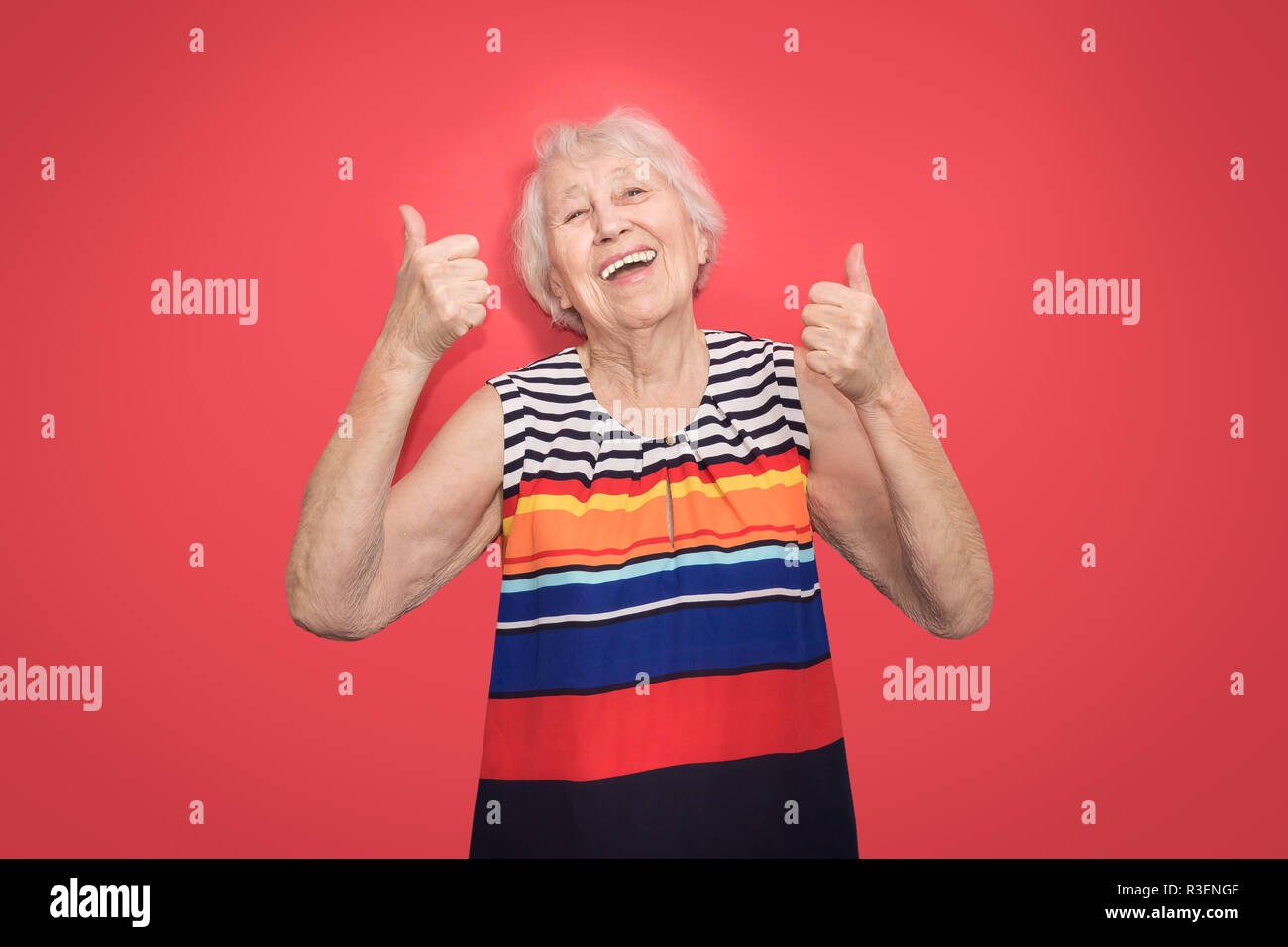 Old smiling woman with surprised expression on her face on red studio ...