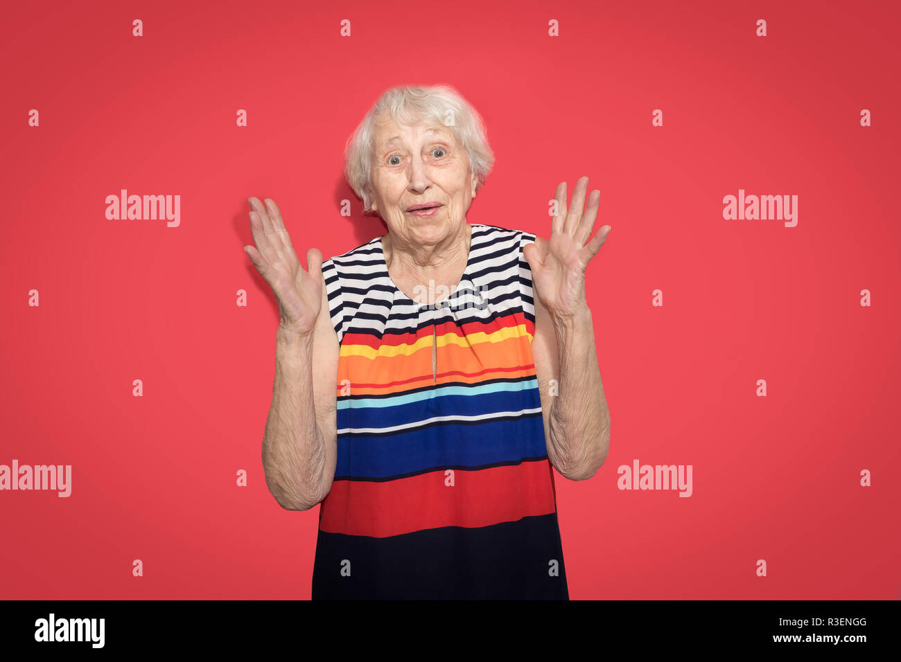 Old smiling woman with surprised expression on her face on red studio ...