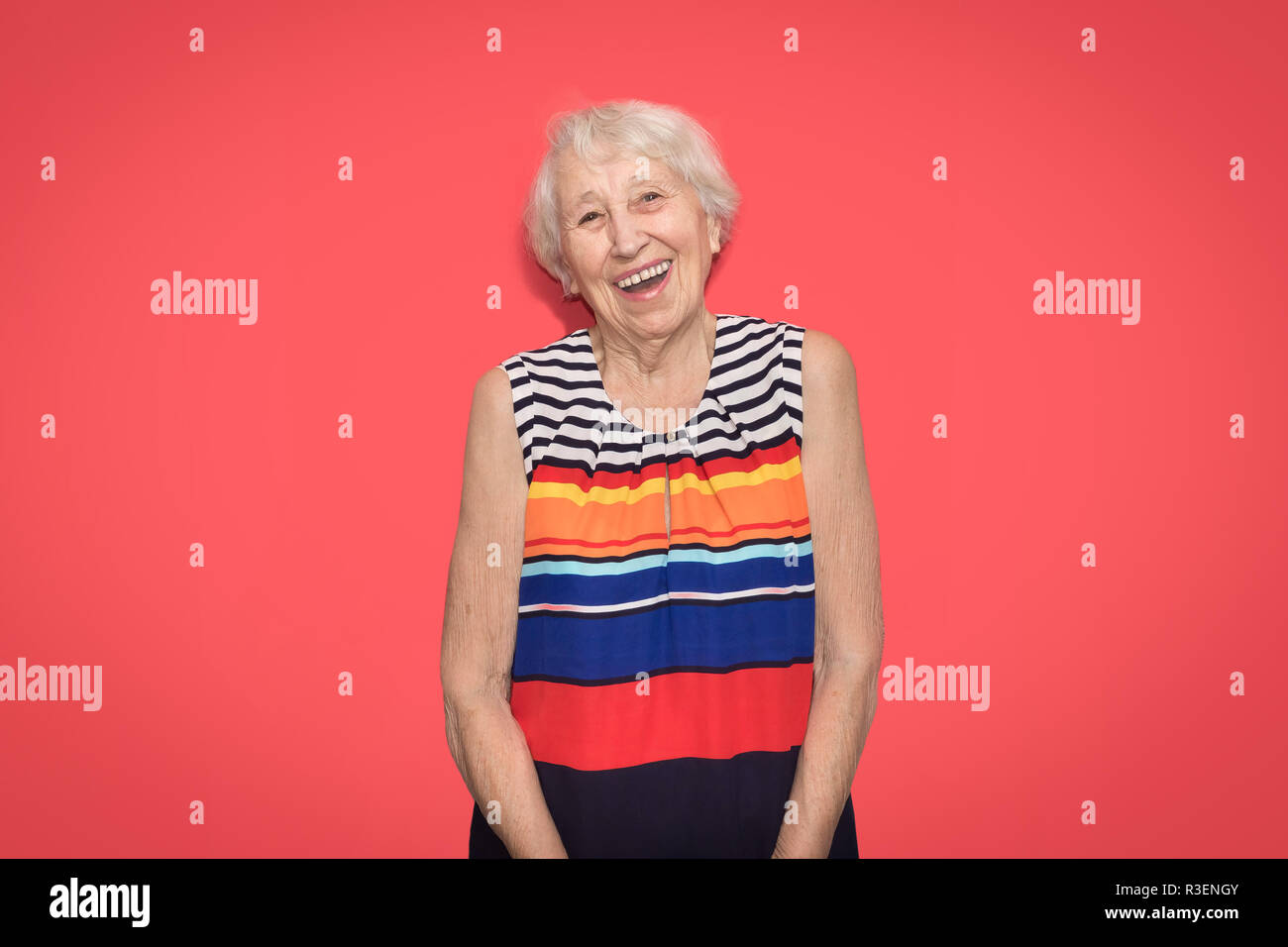 Old smiling woman with happ expression on her face on red studio ...