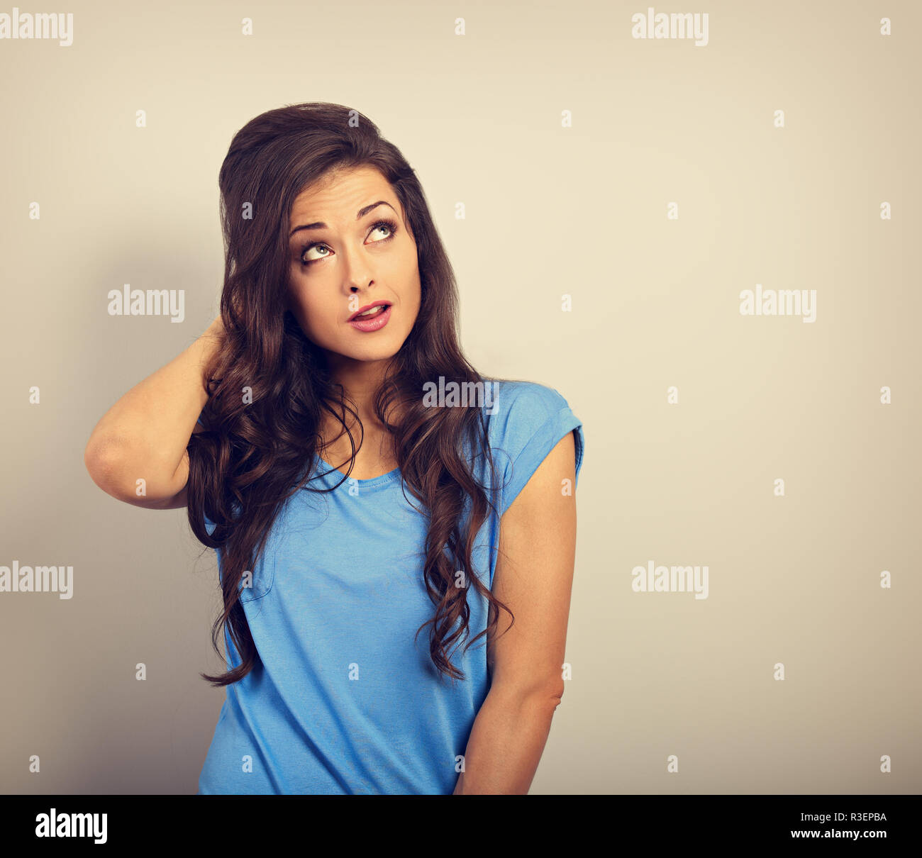 Fun confused grimacing casual woman looking up on blue empty copy space ...