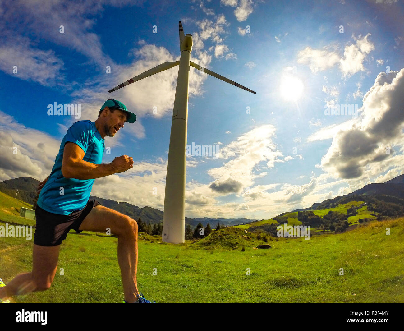 Male athlete running in mountains at wind turbine background Stock ...