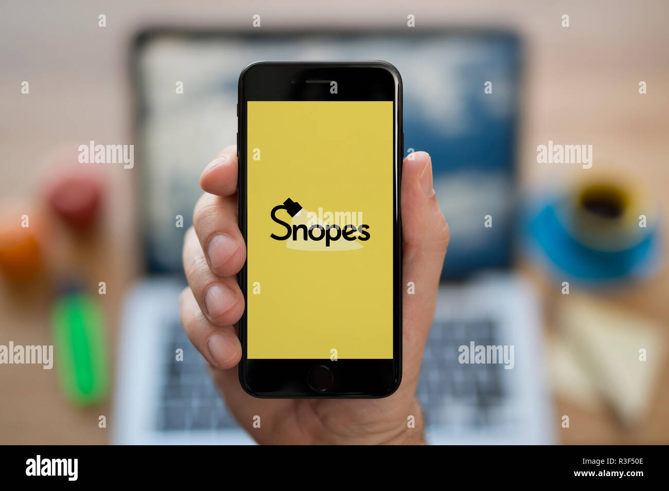 A man looks at his iPhone which displays the Snopes logo, while sat at ...