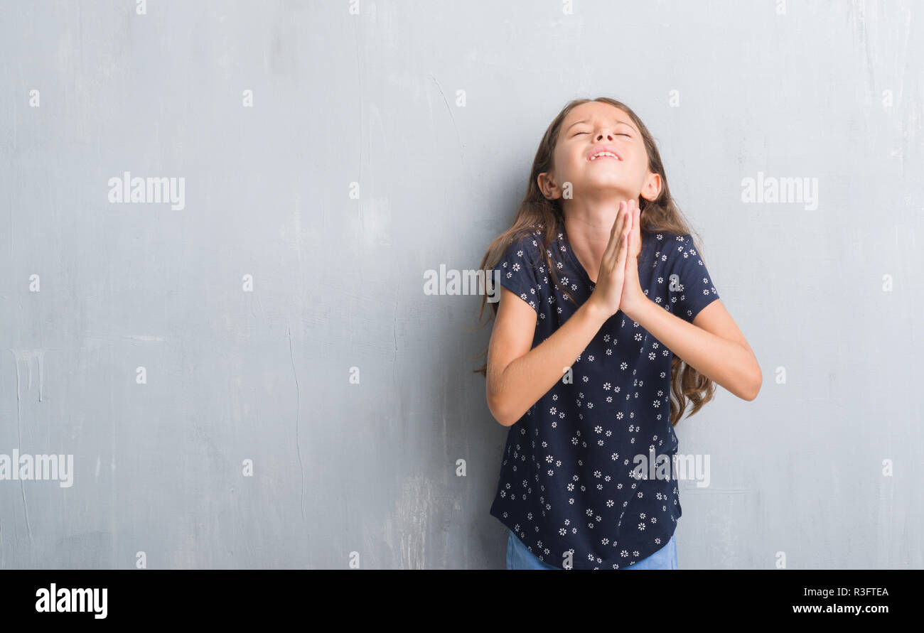 Young hispanic kid over grunge grey wall begging and praying with hands ...