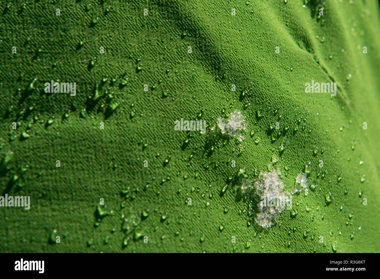 Snow and water droplets on green waterproof fabric from skiing clothes ...