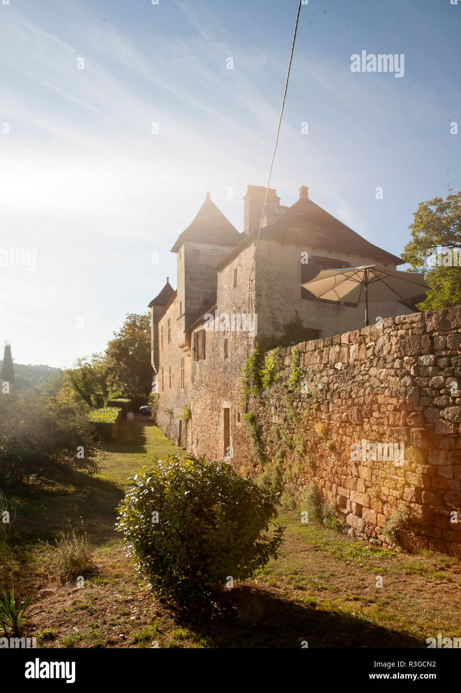 ancient french stone house wall with sun behind it and grass in front ...