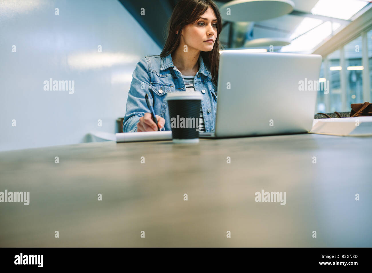 Female student writing information from online research doing homework ...