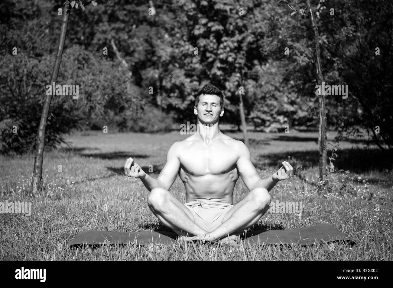 Man with healthy body meditate on yoga mat in summer park. Yoga relax ...