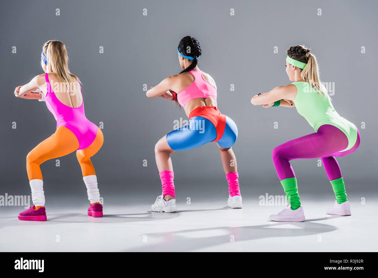 rear view of sporty young women doing squat together on grey Stock ...