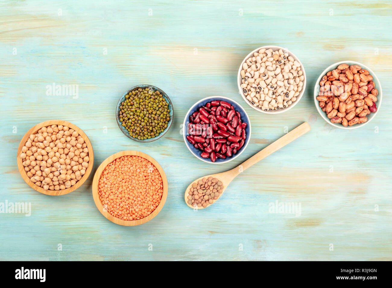 Various types of legumes, shot from the top on a teal background with ...