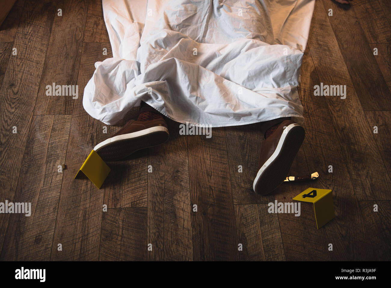 cropped legs of dead dead body covered with white sheet at crime scene ...