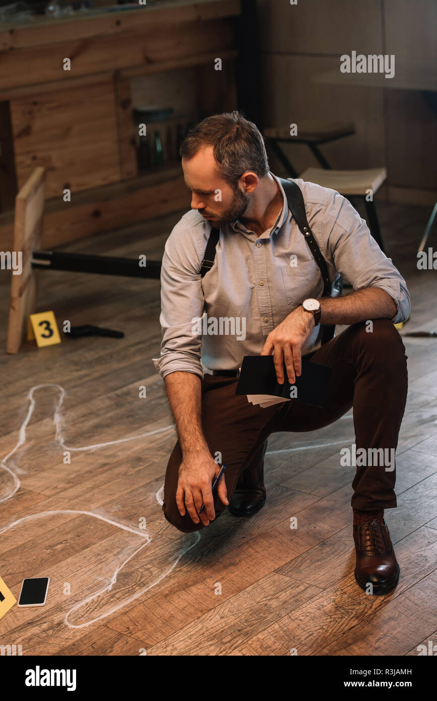Serious Male Detective Sitting At Crime Scene And Looking On Chalk Line