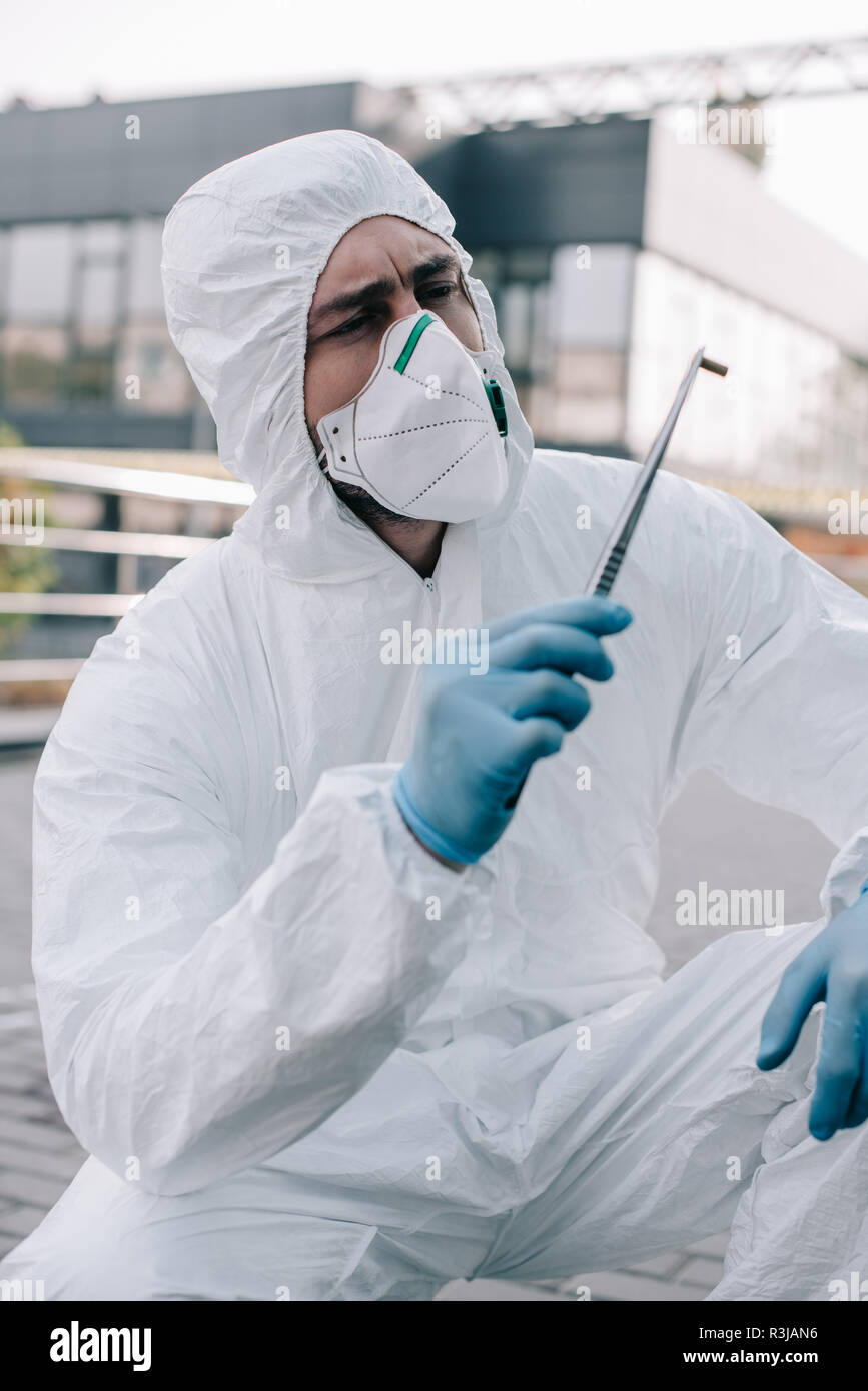 Male Criminologist In Protective Suit And Latex Gloves Looking At