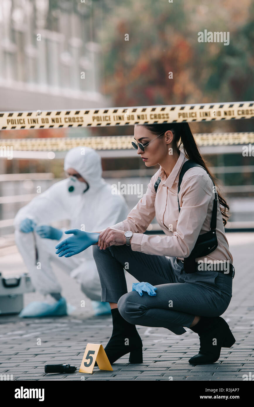 Female Detective In Sunglasses Wearing Latex Gloves With Criminologist