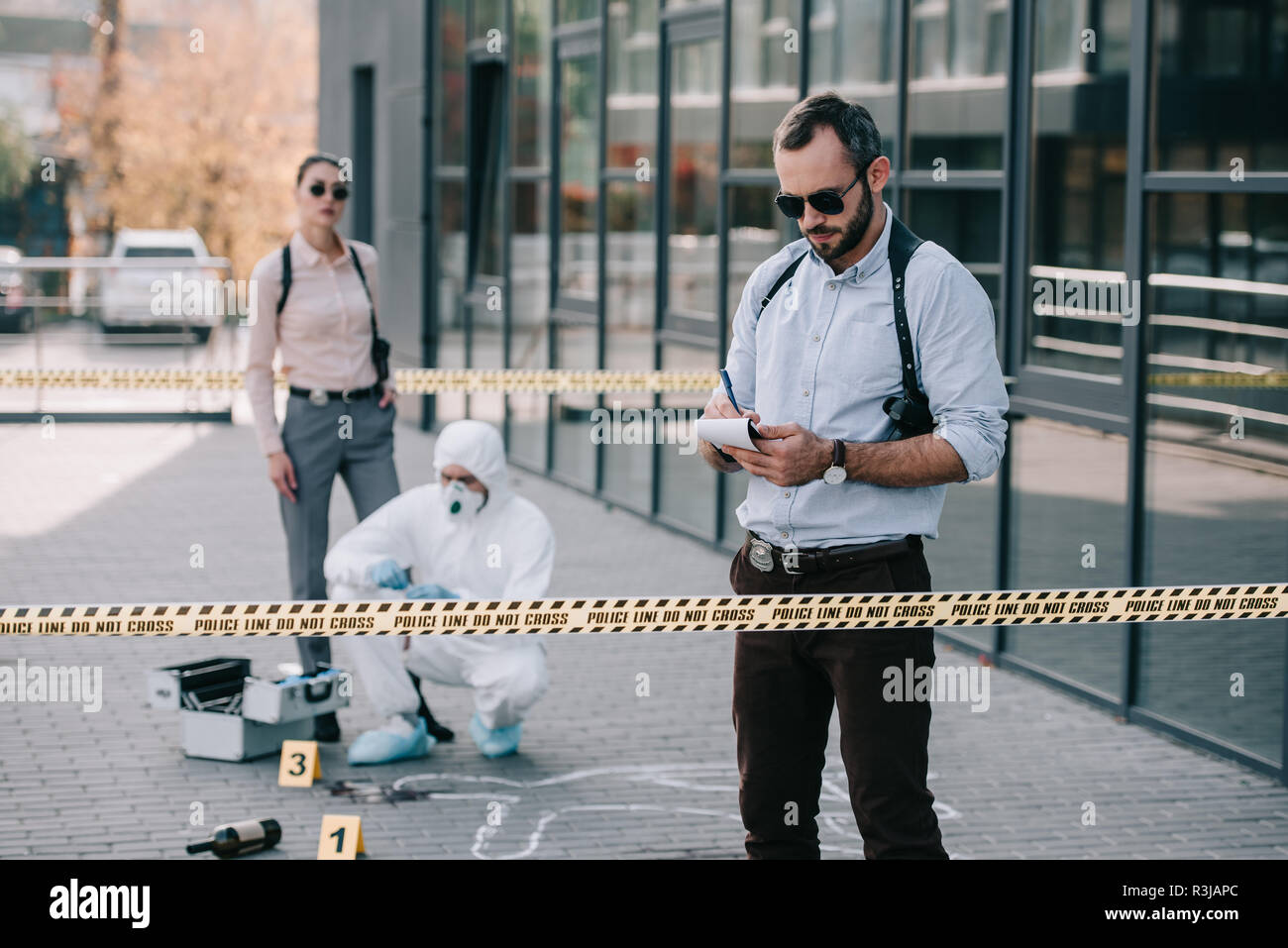 male detective standing at crime scene and making notes in his notebook ...