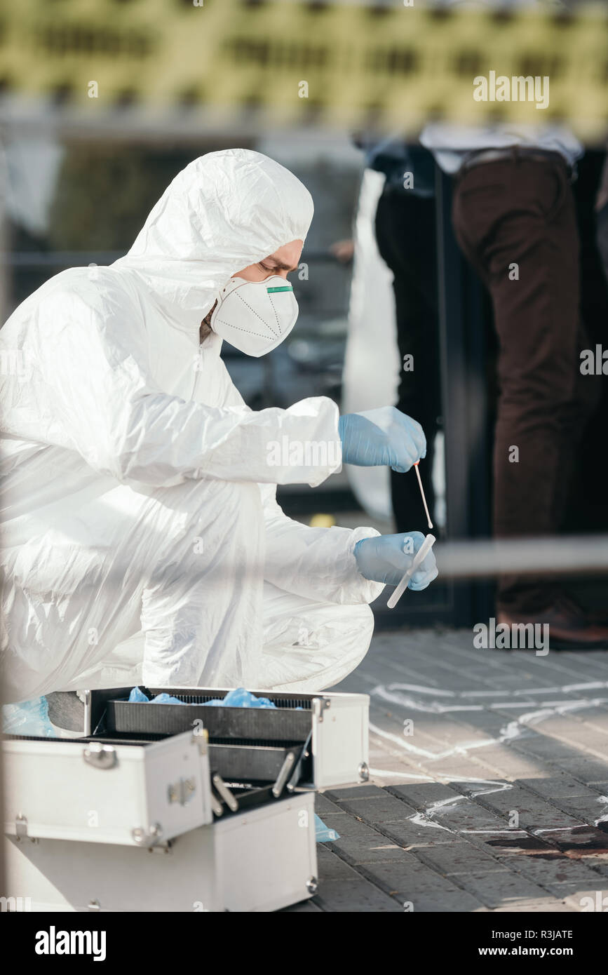 male criminologist in protective suit and latex gloves collecting blood ...