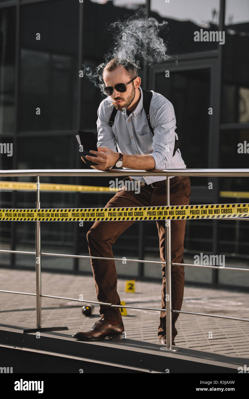 male detective smoking and looking at notes leaning on the fence Stock ...