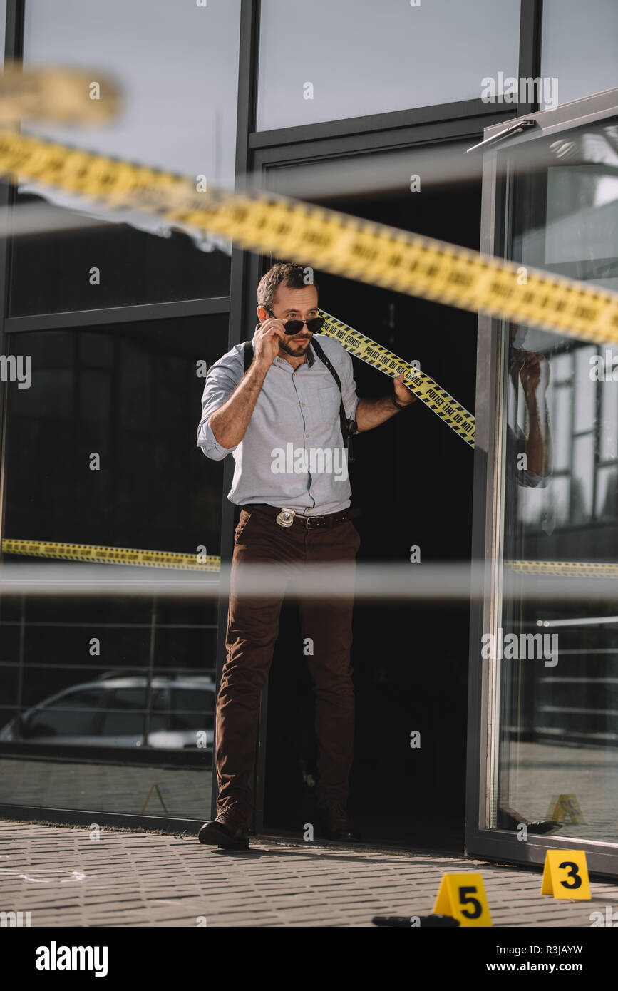 male detective coming out of the building straightening sunglasses ...