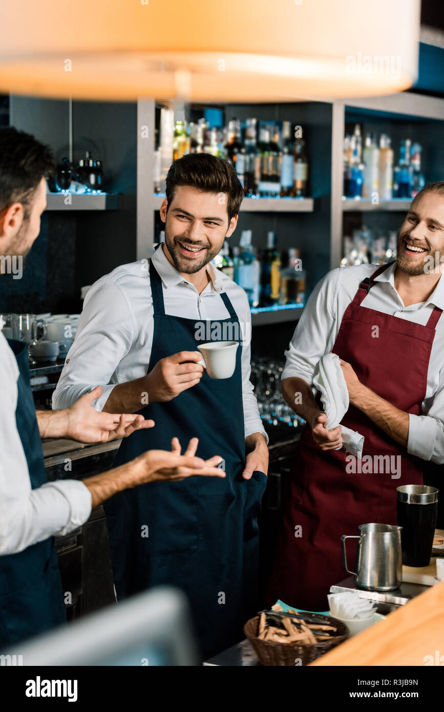 smiling barman drinking coffee and talking to colleagues at workplace ...