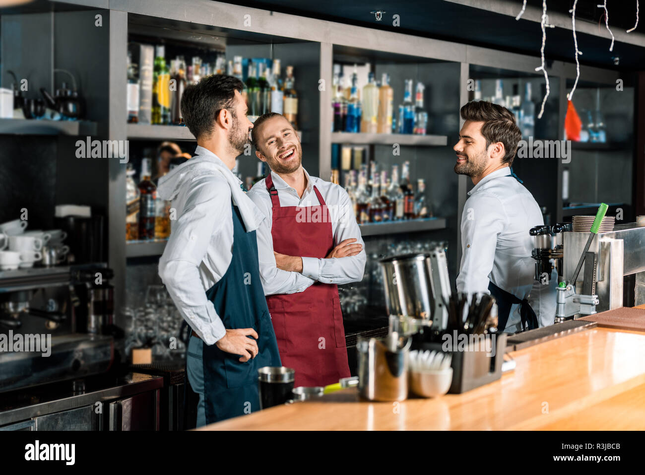cheerful happy handsome barmen in aprons talking at workplace Stock ...