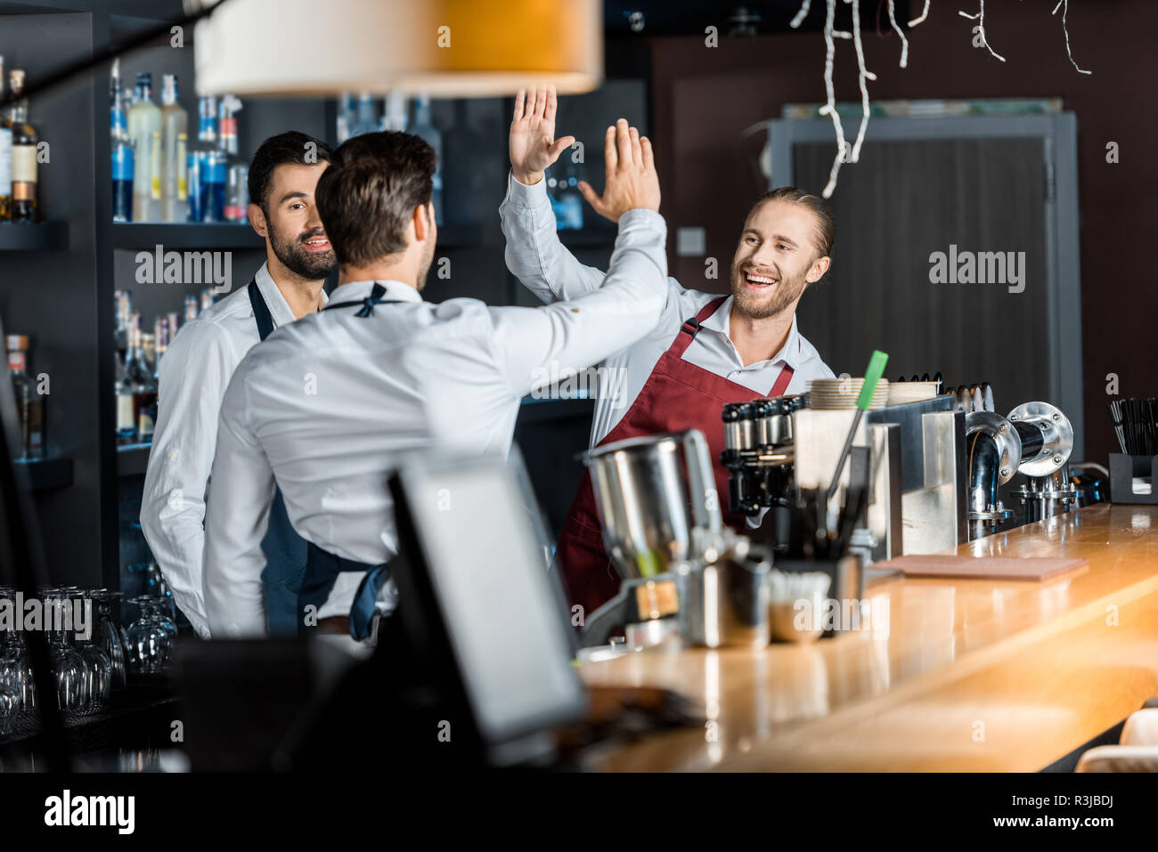 handsome smiling barmen in aprons high five at workplace Stock Photo ...