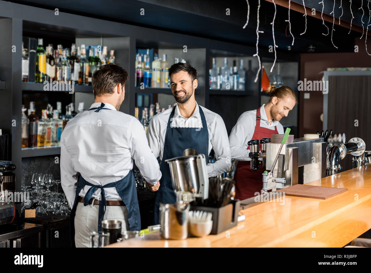 adult barmen in aprons shaking hands near counter Stock Photo - Alamy
