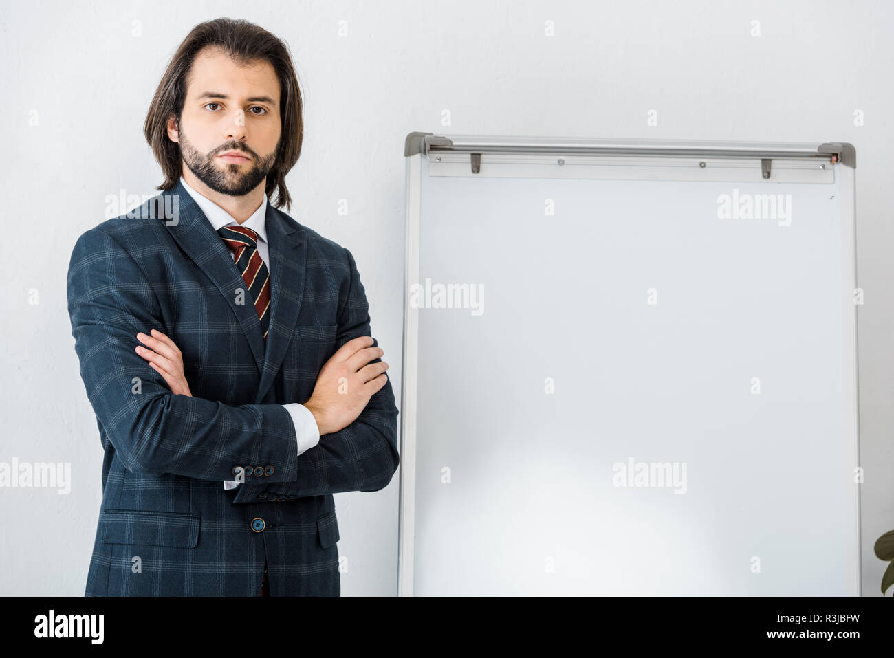 young serious male insurance agent standing with arms crossed near ...