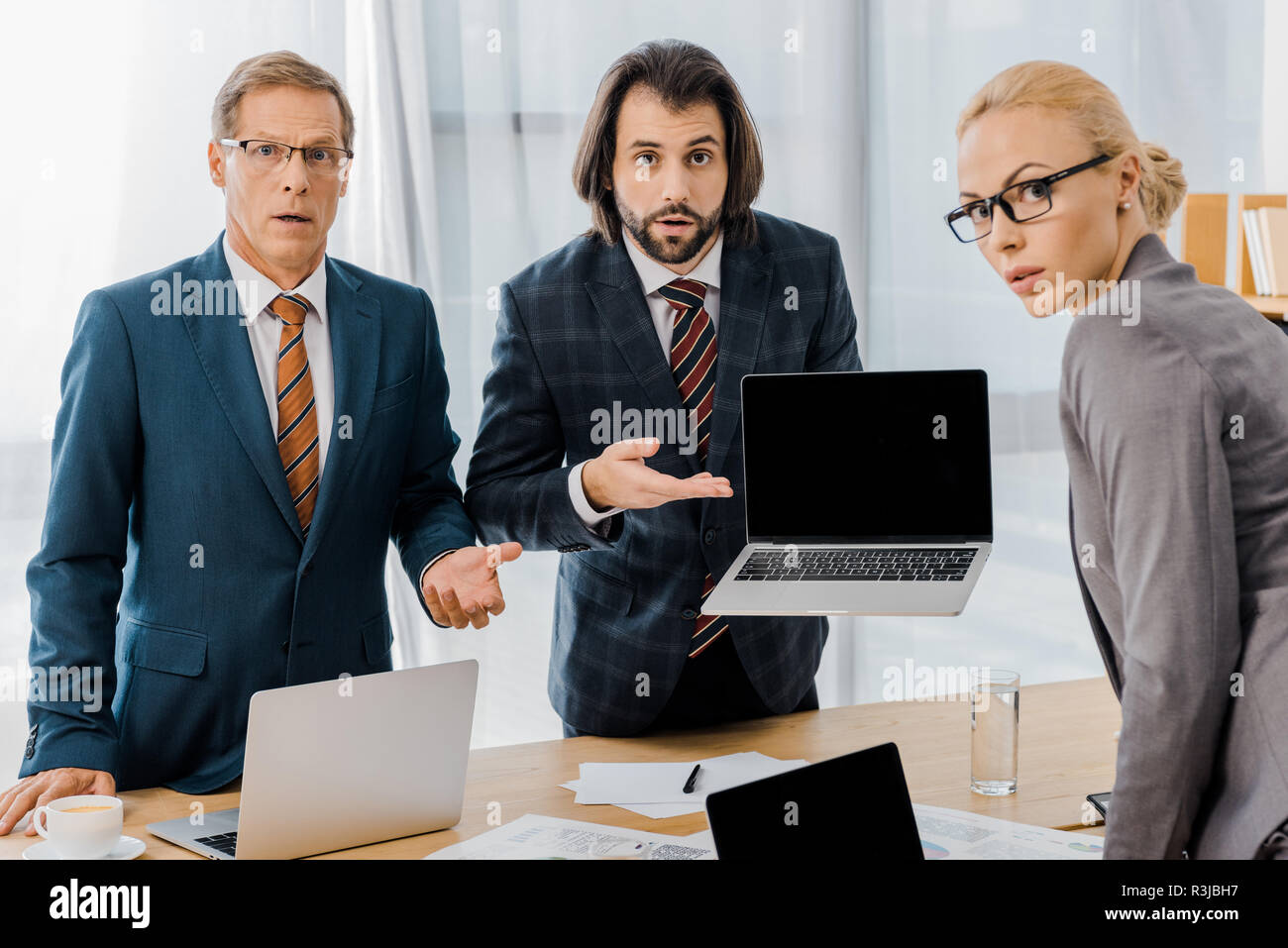 young serious male insurance agent standing with workers and pointing ...