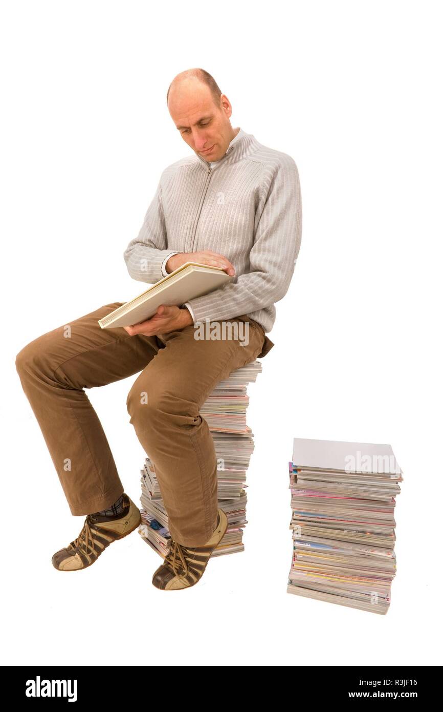 man sitting on a stack of magazines and looking at a book Stock Photo ...