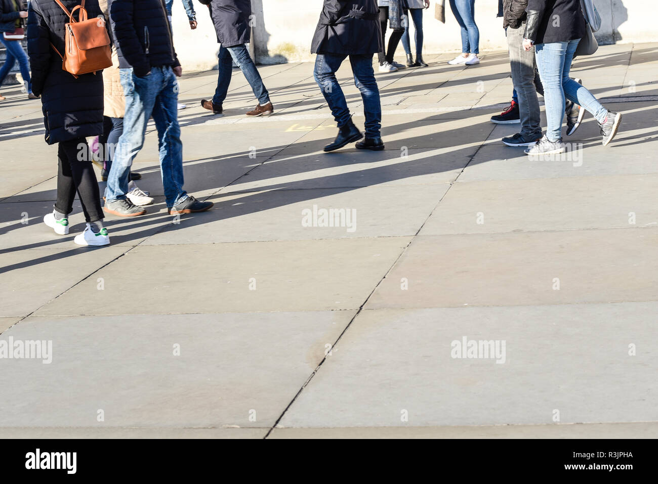 Long shadows of walkers walking on bright concrete slab paving in low ...