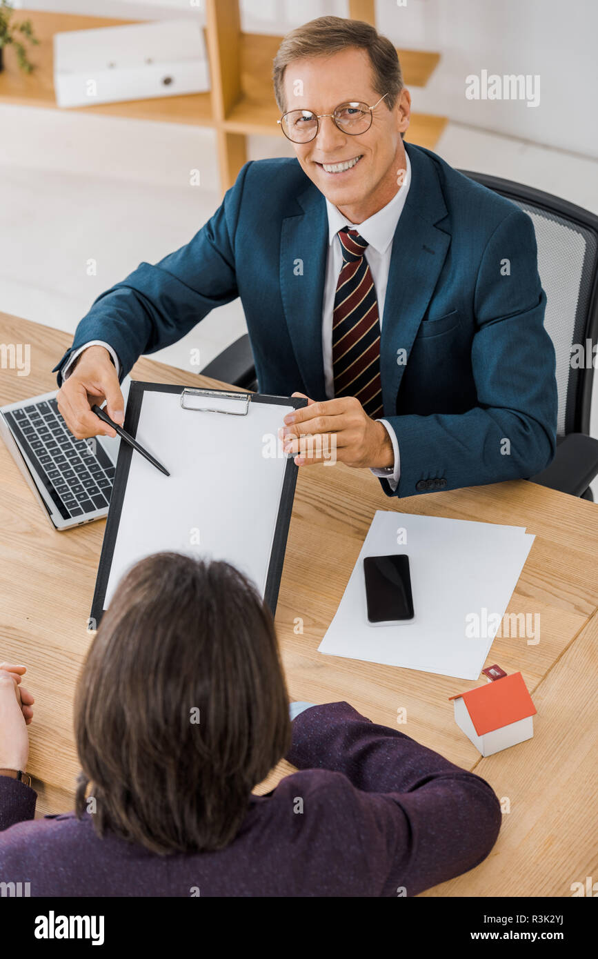 adult smiling insurance agent in glasses showing contract to young man ...