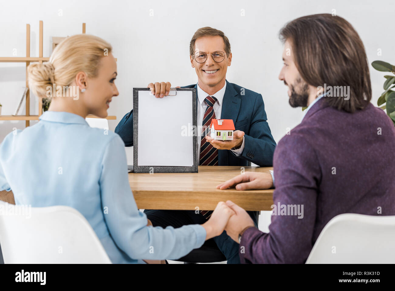 happy couple holding hands while insurance agent showing contract and ...