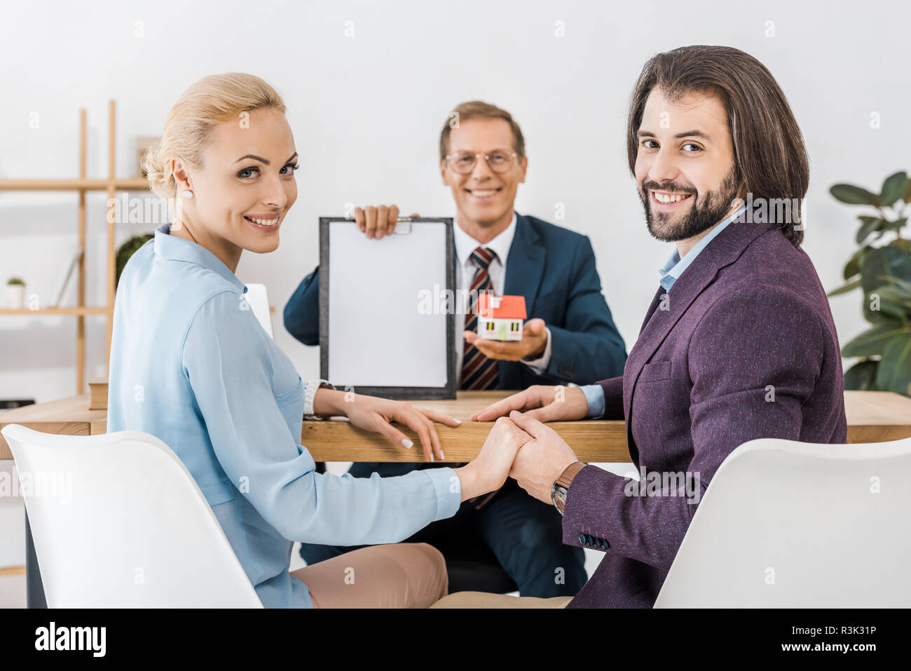 happy couple holding hands while insurance agent showing contract and ...