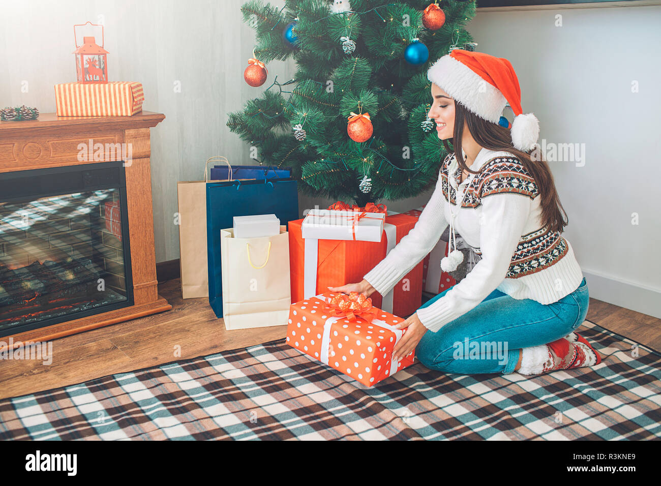 Beautiful brunette sits in squad position at Christmas tree with ...