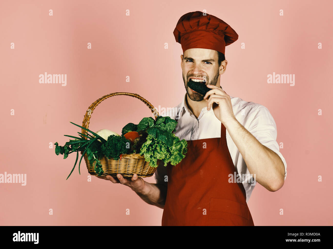 Chef in burgundy uniform eats cucumber. Vegetarian cuisine concept. Man ...