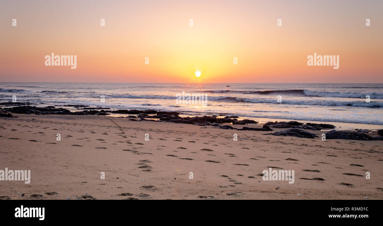 Footprints on the sand lead towards the ocean during sunset. Clear sky ...