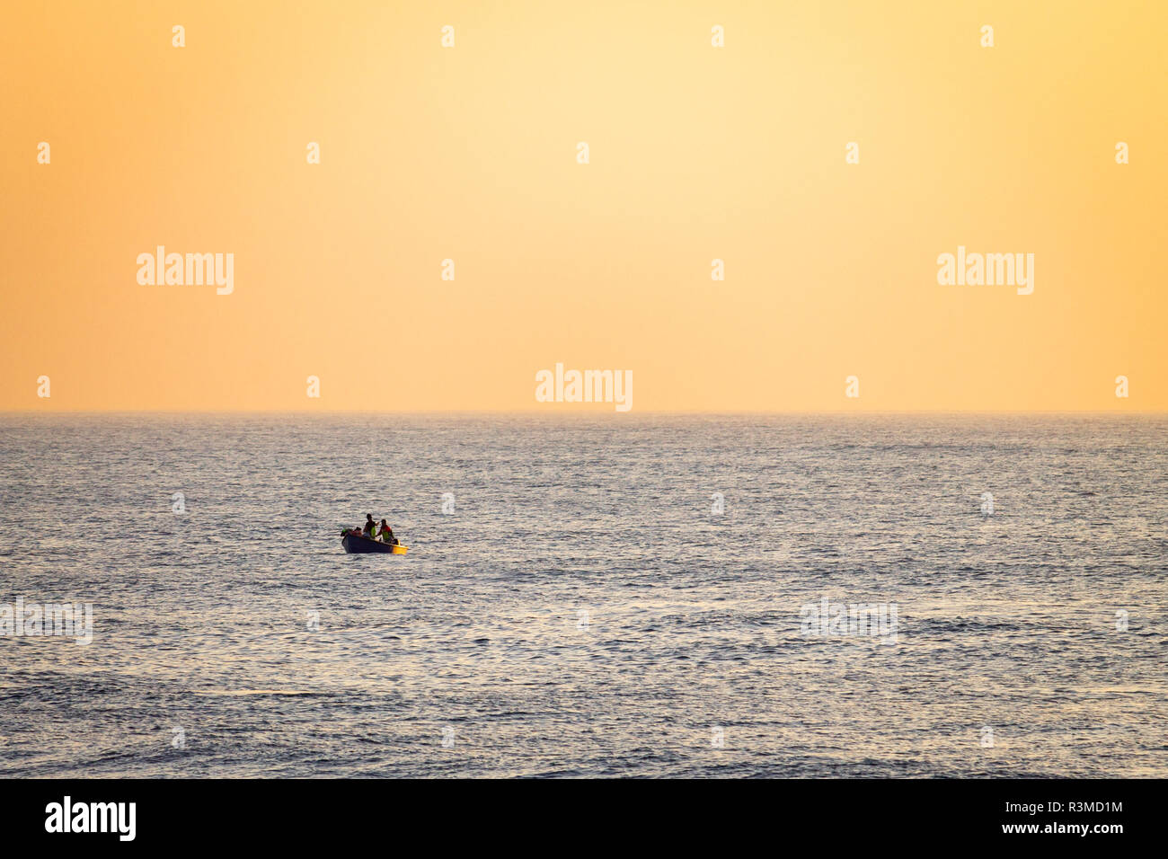 Distant isolated lonely boat with two men sails in the ocean. Golden ... Distant isolated lonely boat with two men sails in the ocean. Golden ...
