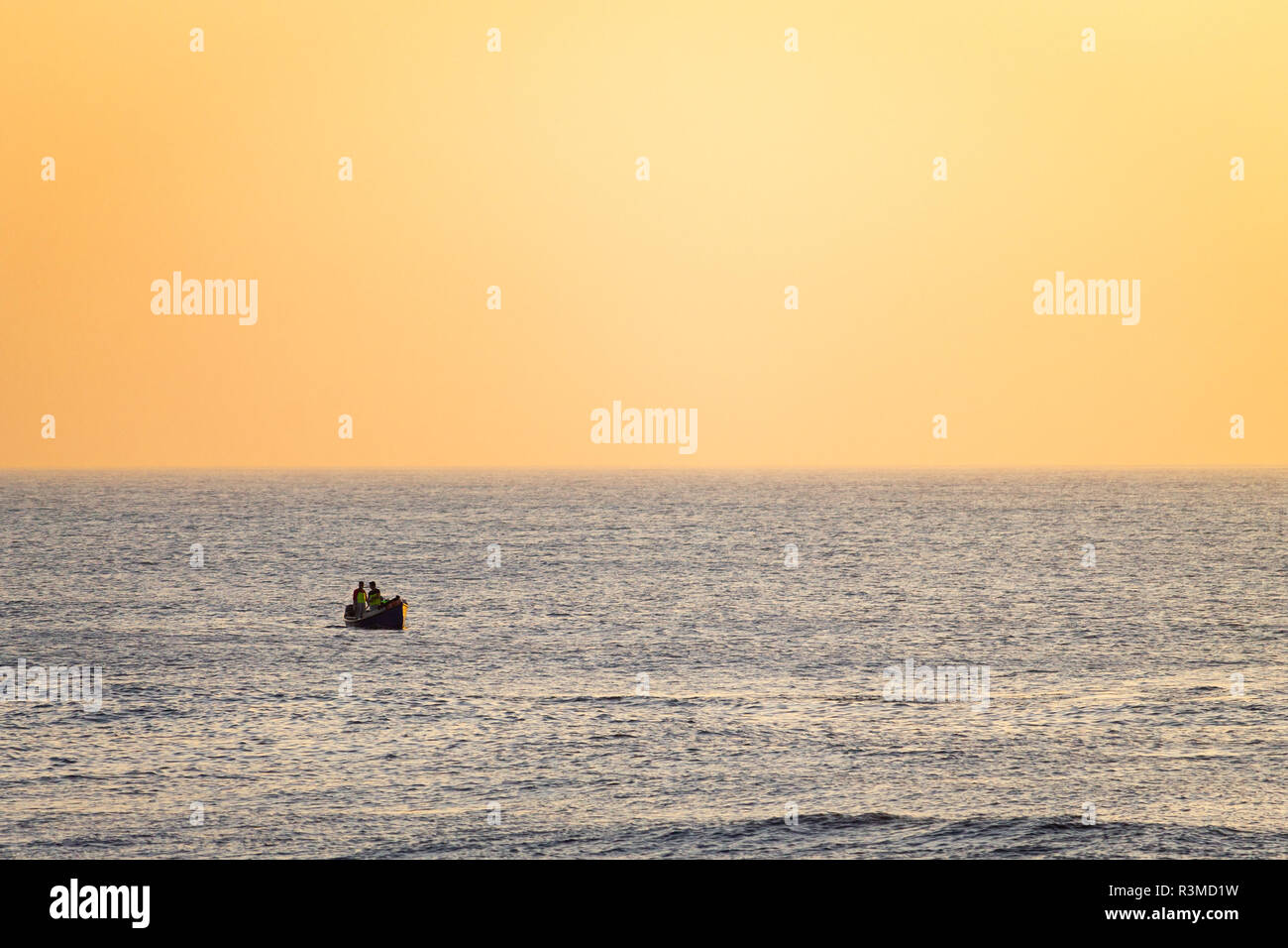 Distant isolated lonely boat with two men sails in the ocean. Golden ... Distant isolated lonely boat with two men sails in the ocean. Golden ...